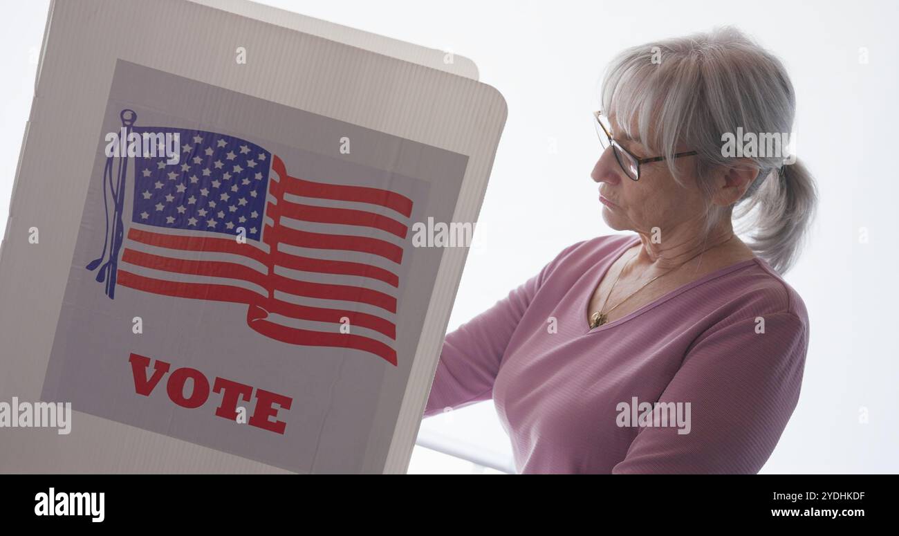 Senior woman casting votes at booth with white background behind ...