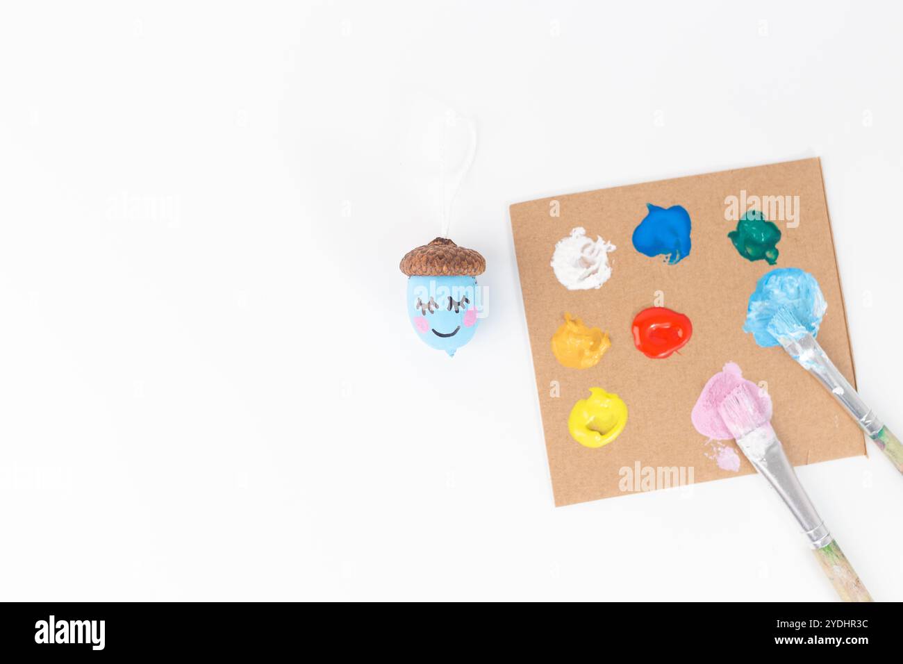 Colorful hand painted acorn next to a paint palette and brushes on a ...