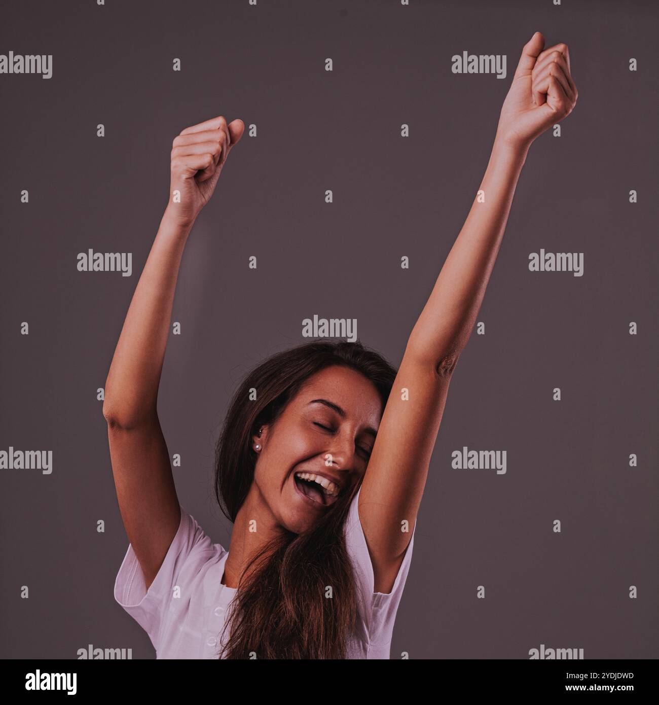 Excited young woman in white t shirt celebrates success with arms ...
