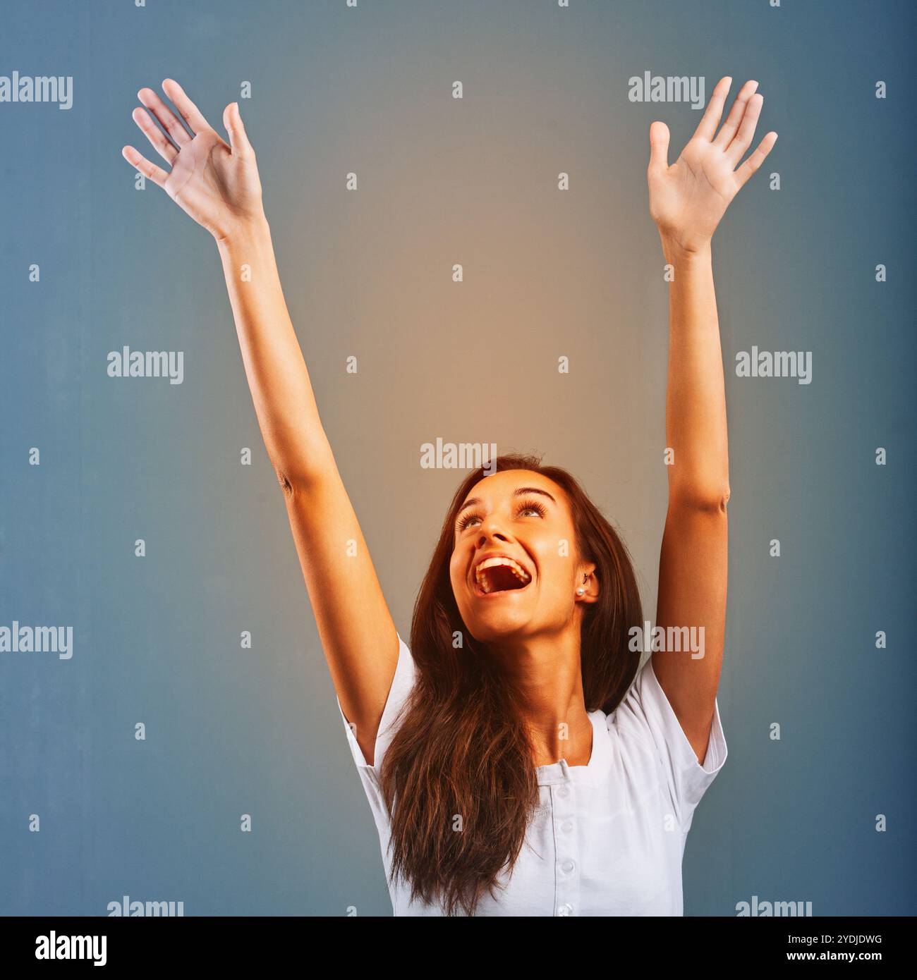 Excited young latin woman raising her arms and cheering with open mouth and closed eyes ...