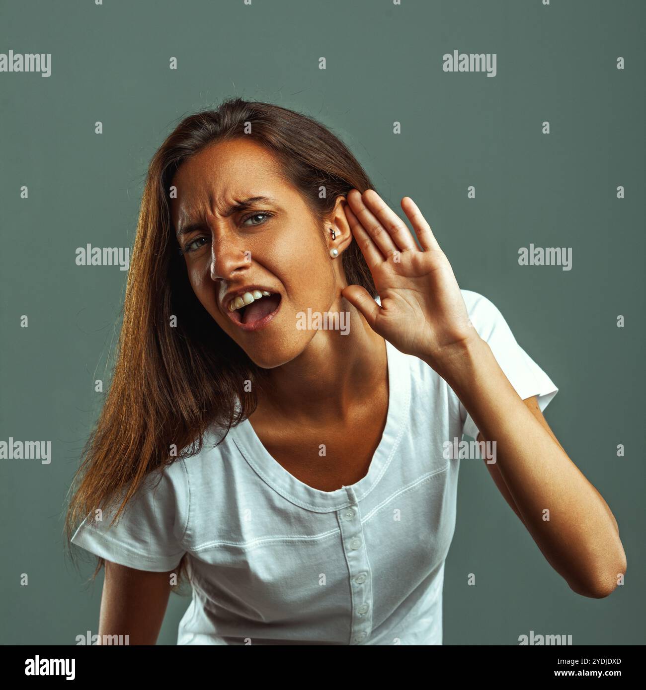 Curious woman in white shirt listening intently, hand to ear, on gray background Stock Photo - Alamy