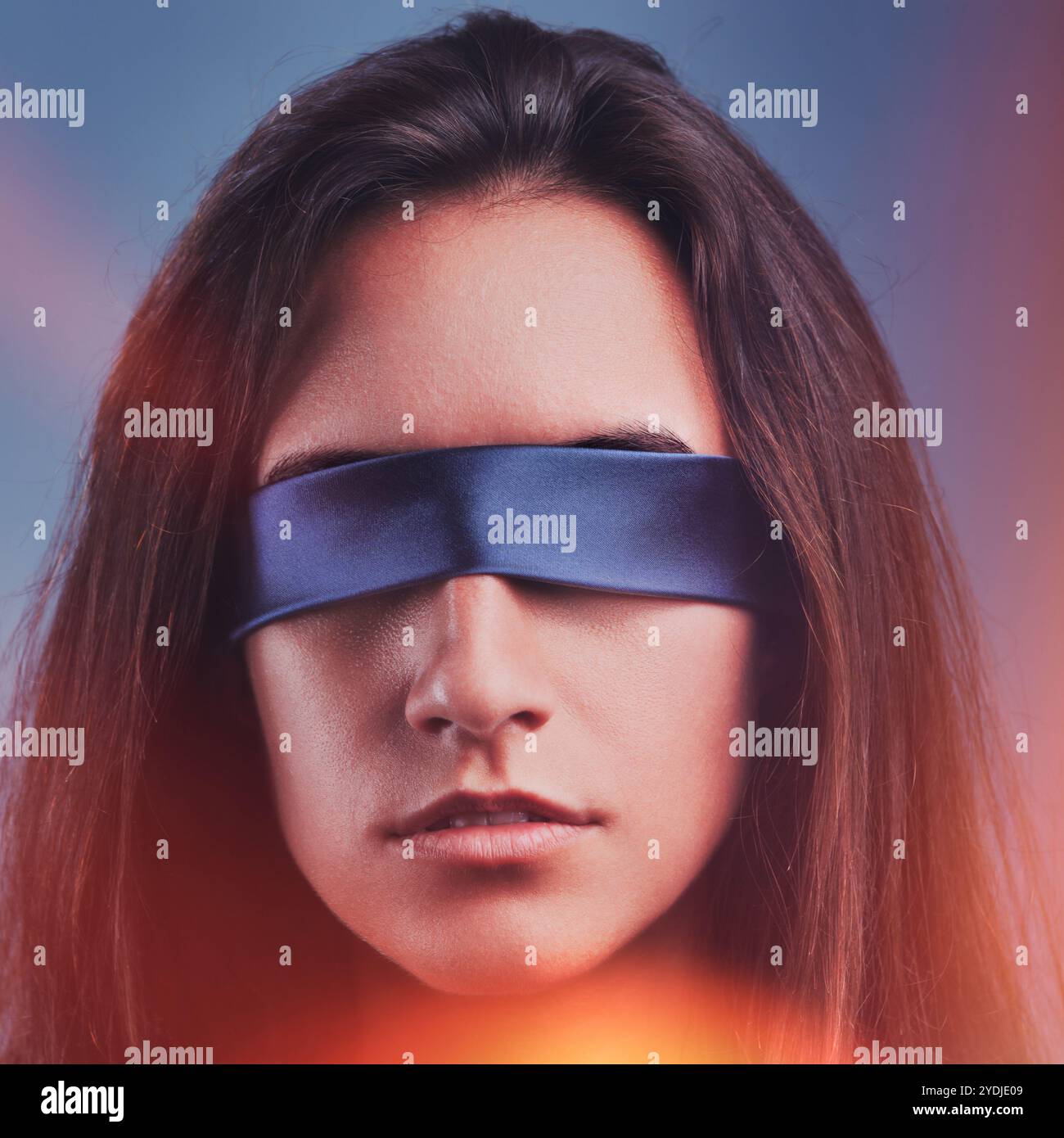 Studio portrait of a young woman with long brown hair, wearing a blue satin blindfold over her ...