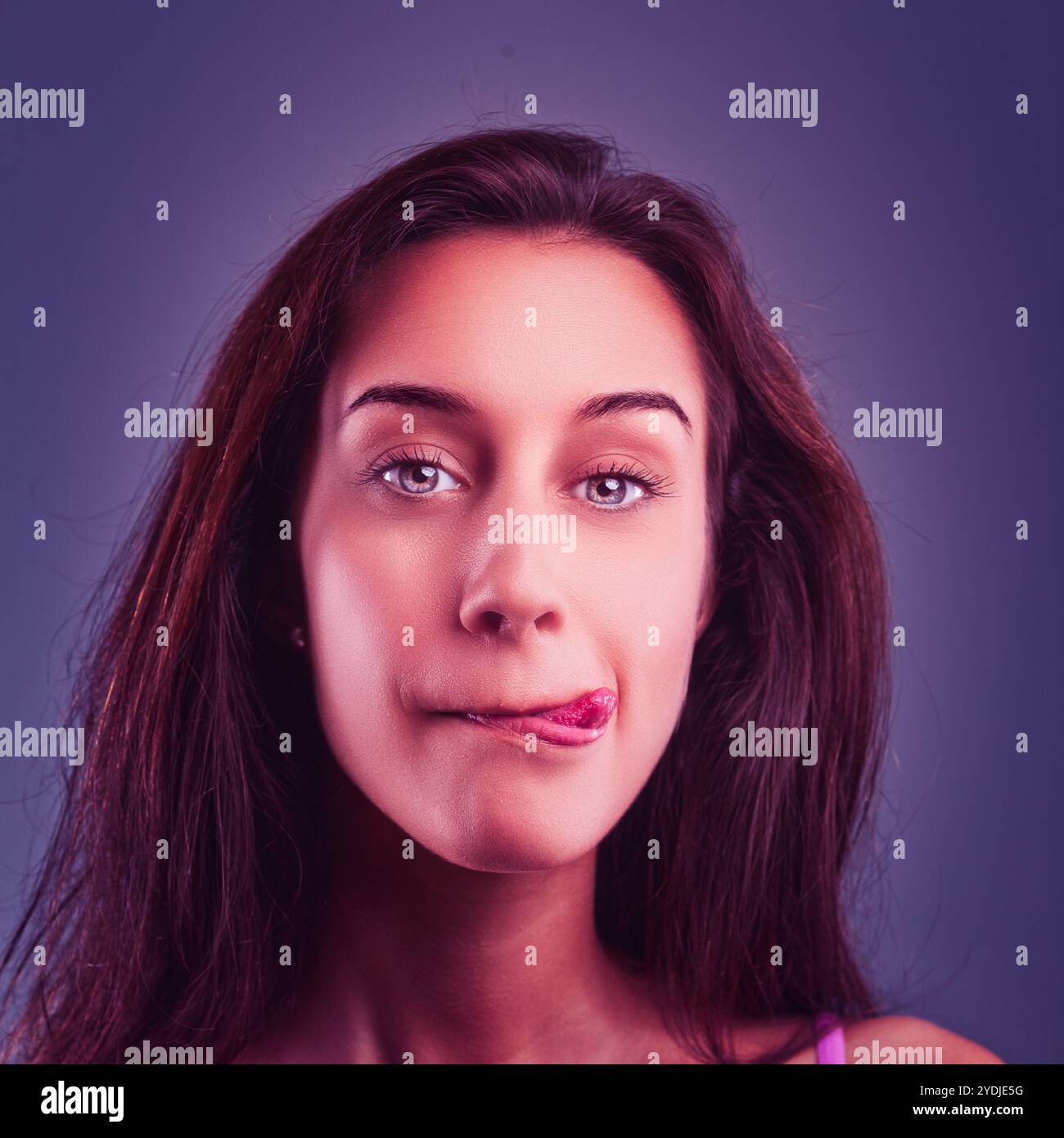 Portrait of a young woman biting her lip on a purple background ...