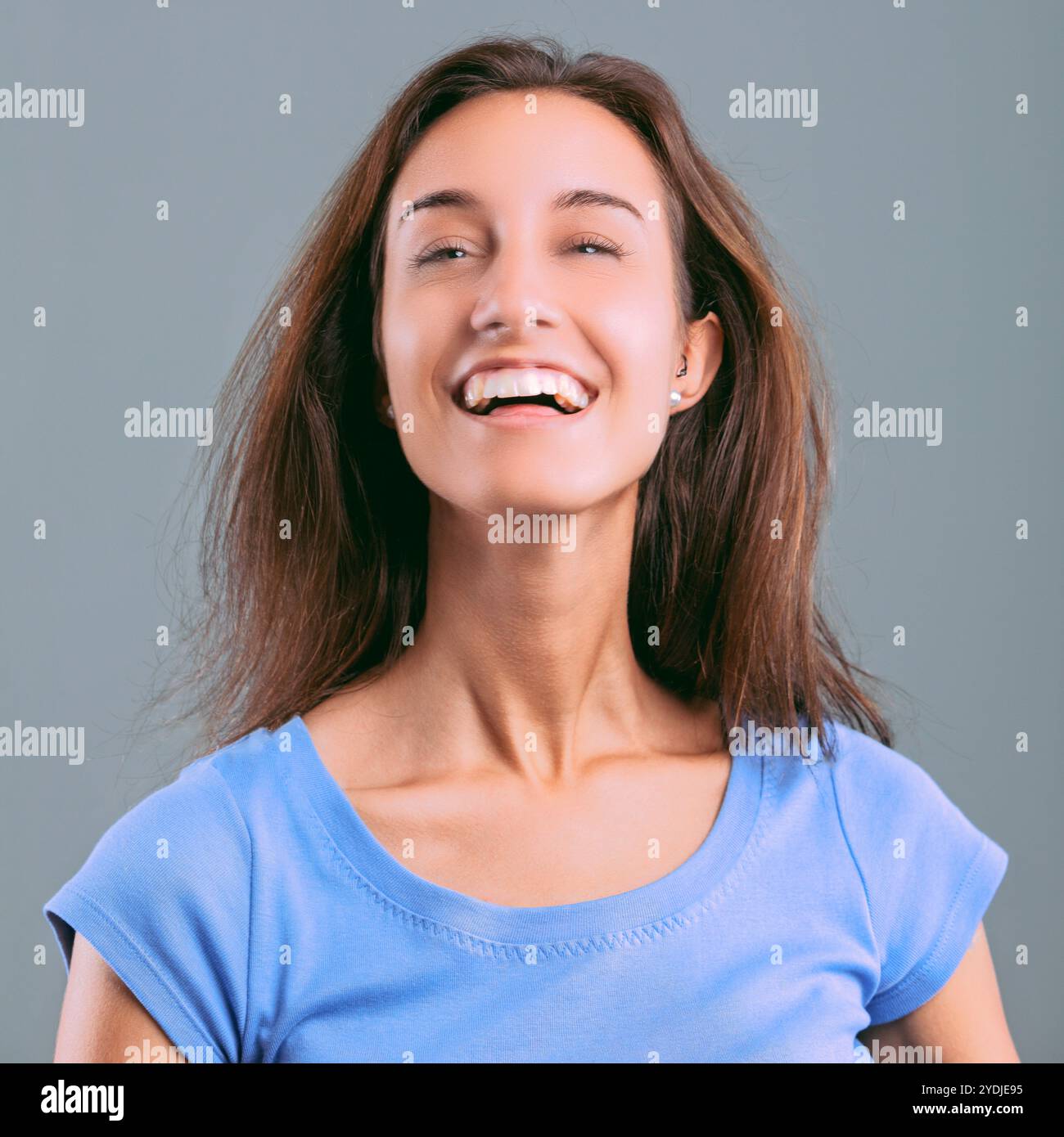 Expressing pure joy and happiness, a young woman laughs with her eyes closed and head tilted ...