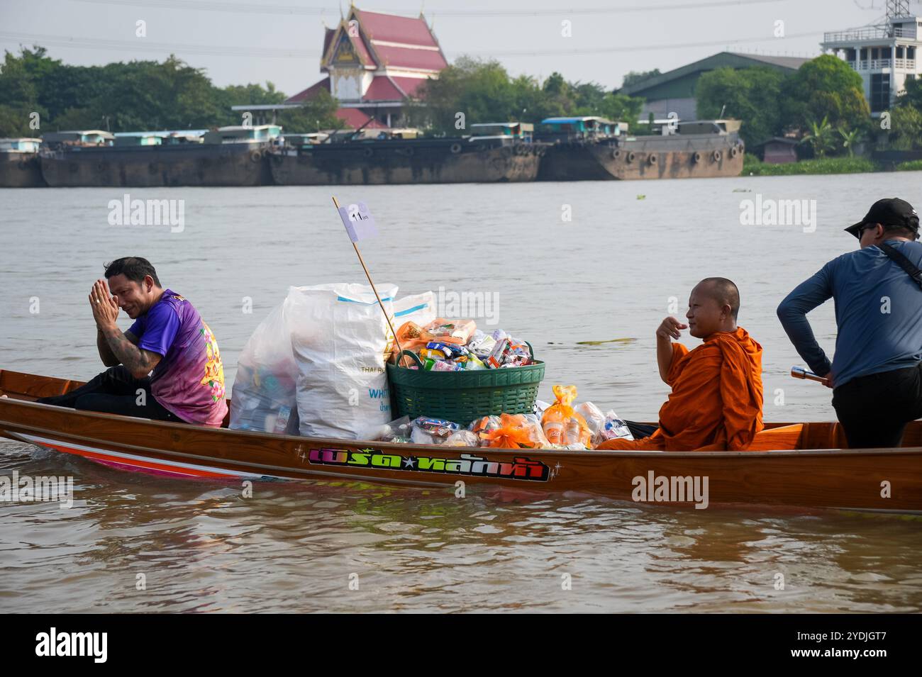 A monk is seen sitting on a rowboat with baskets of offerings while a ...