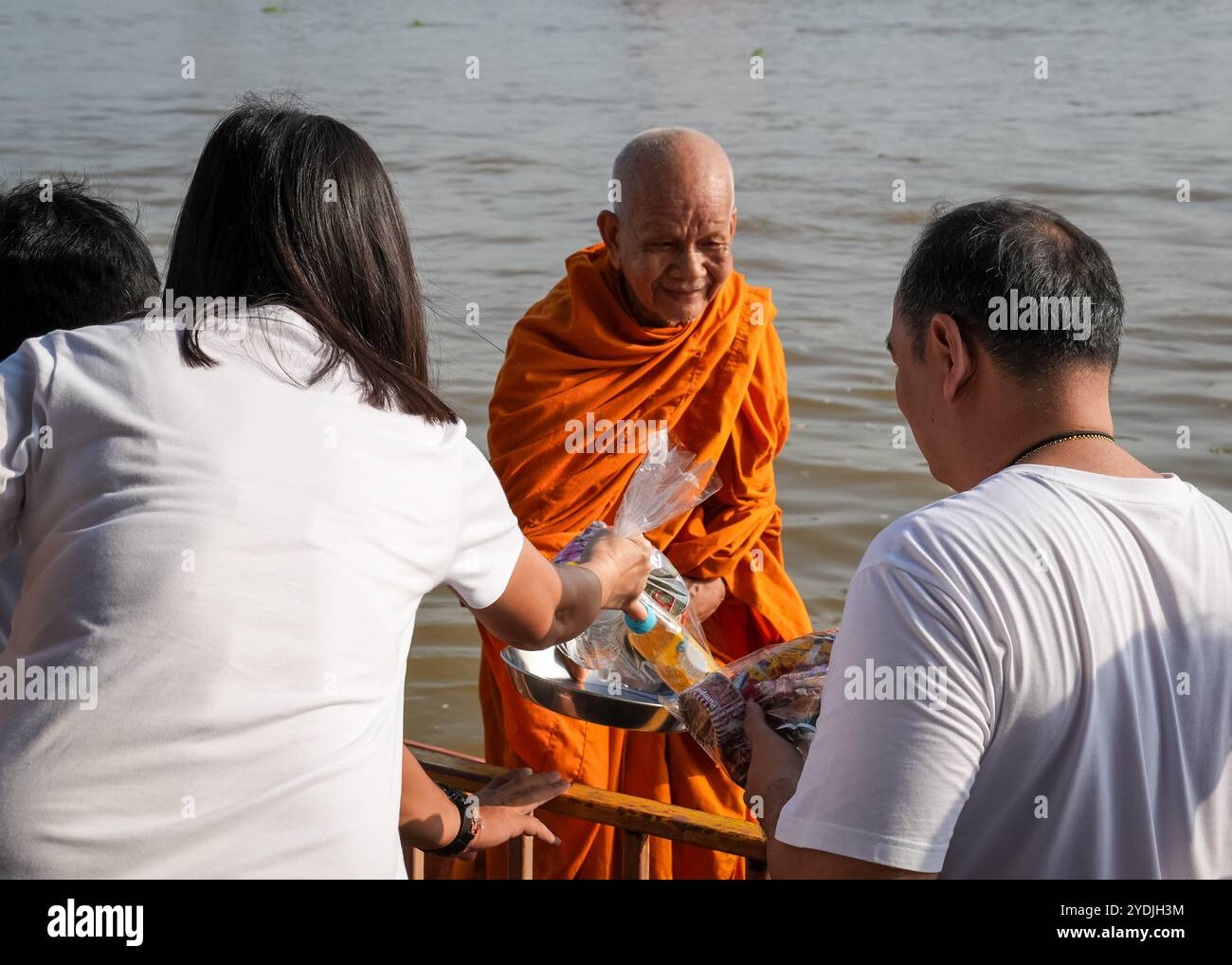 A close-up of a smiling monk receiving offerings from people, on the ...