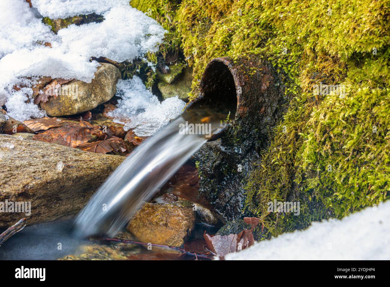 A stream of water flows from a pipe in a snowy landscape, close-up view ...