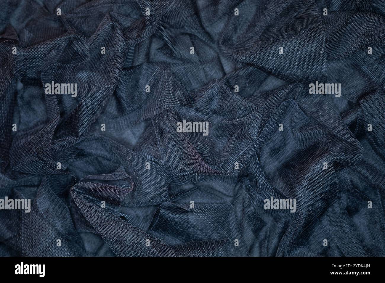 A dark fabric lays draped across a surface, revealing its rich textures ...