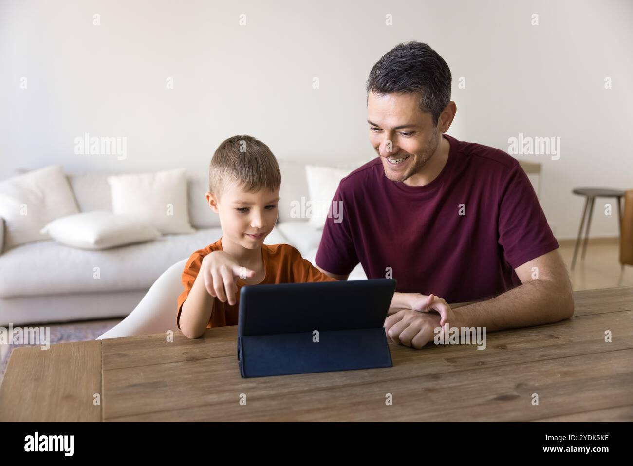 Positive dad teaching little son to use service on tablet Stock Photo ...
