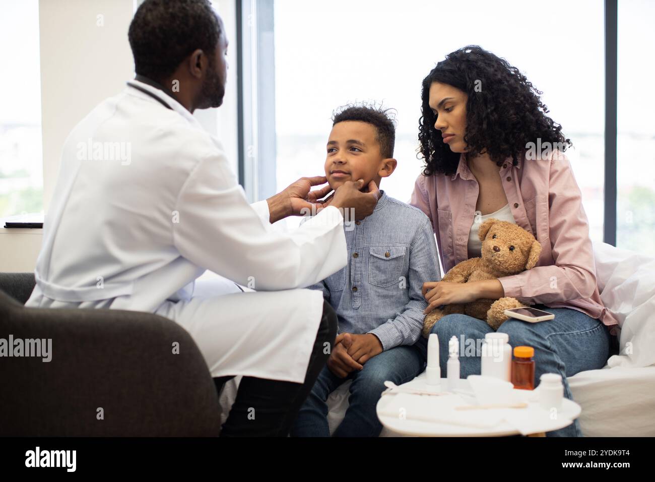 African doctor examines young African boy's lymph nodes while seated by ...