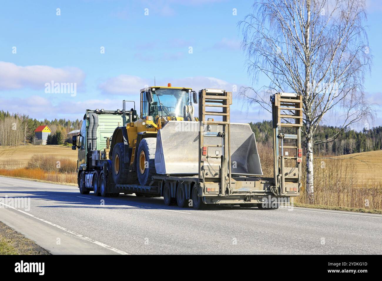 Truck transports large wheel loader on low loader semi trailer along ...