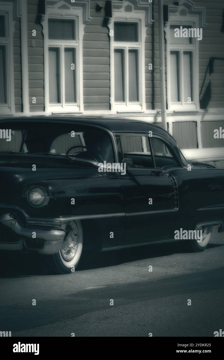 Classic car driving along street, old wooden building on the background ...