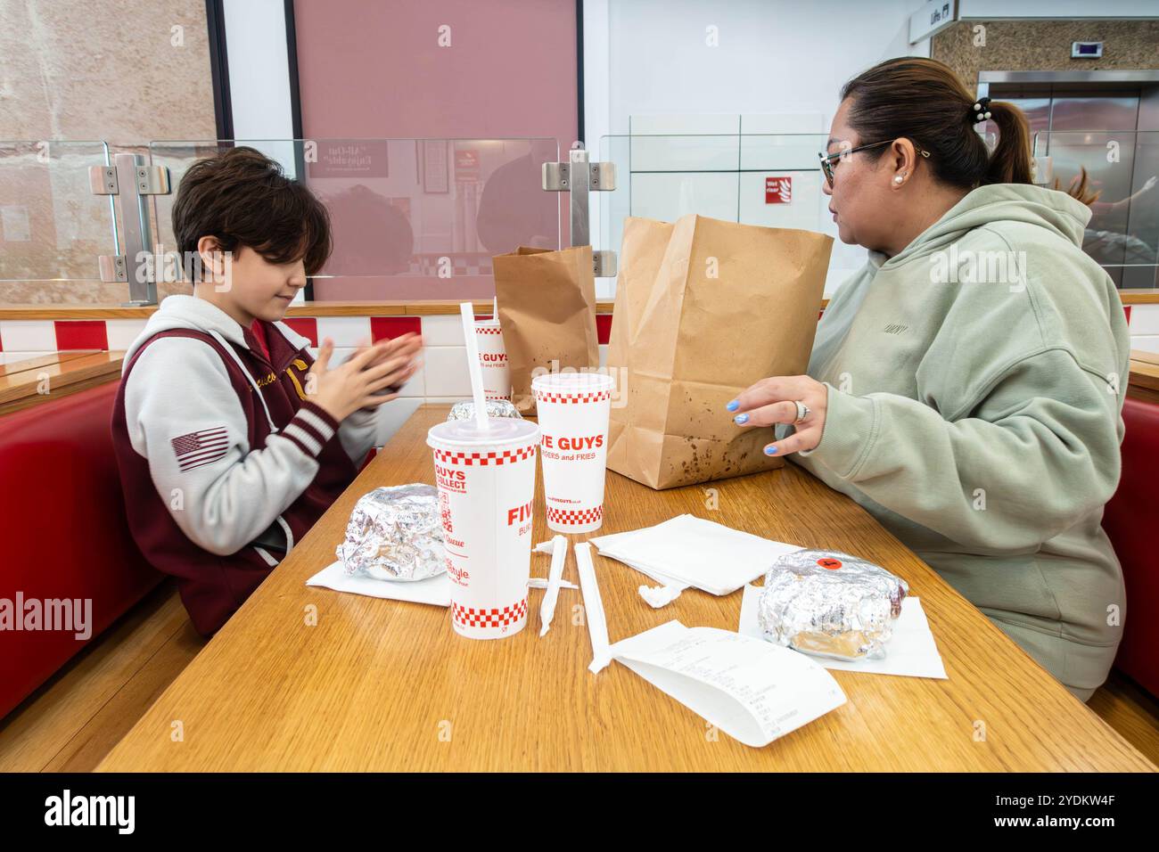 Mother and son sit together at a table in a Five Guys restaurant ready ...