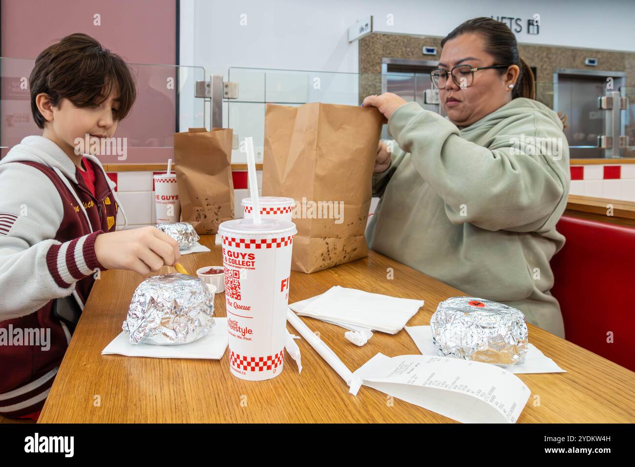 Mother and son sit together at a table in a Five Guys restaurant ready ...