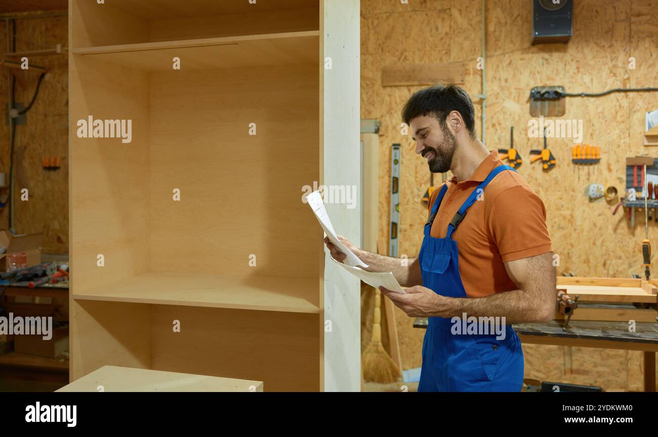 Carpenter looking at paper sheet with project blueprint at woodshop ...