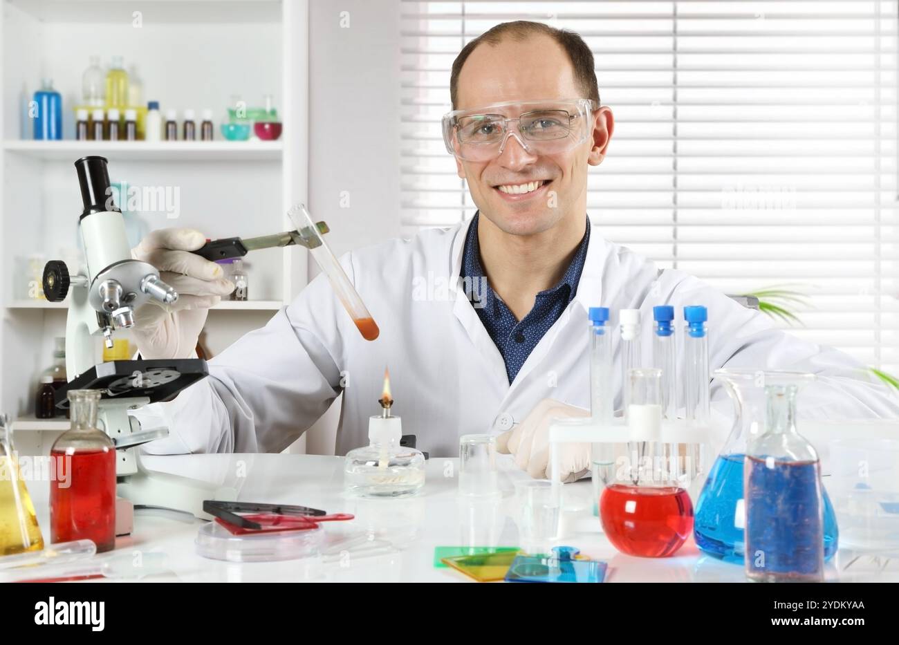 Happy young scientist in goggles and a white coat is conducting ...