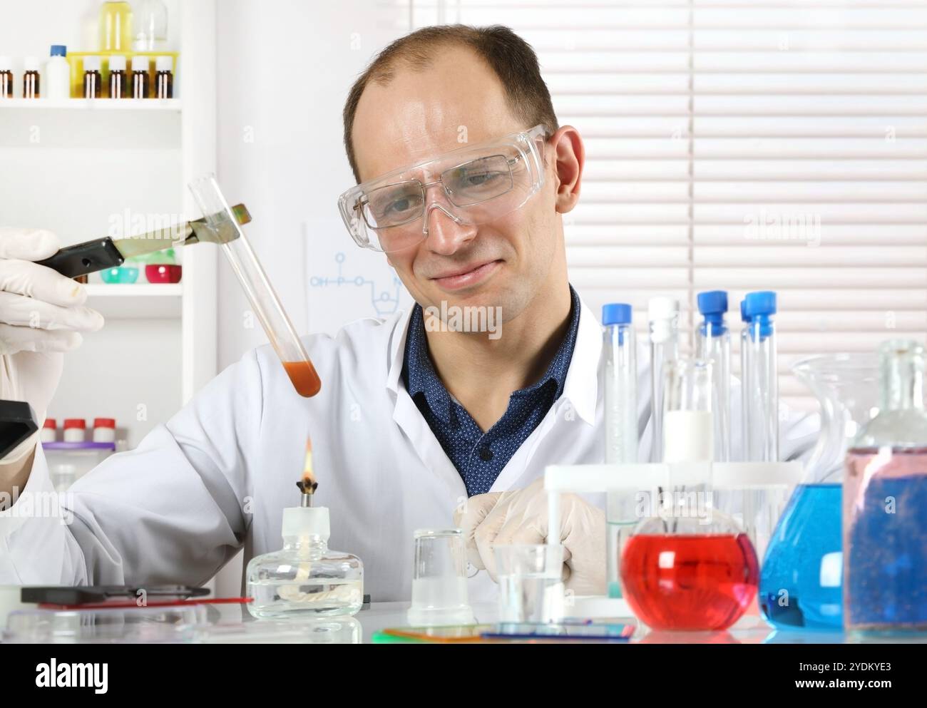 Young scientist in goggles and a white coat is conducting experiments ...