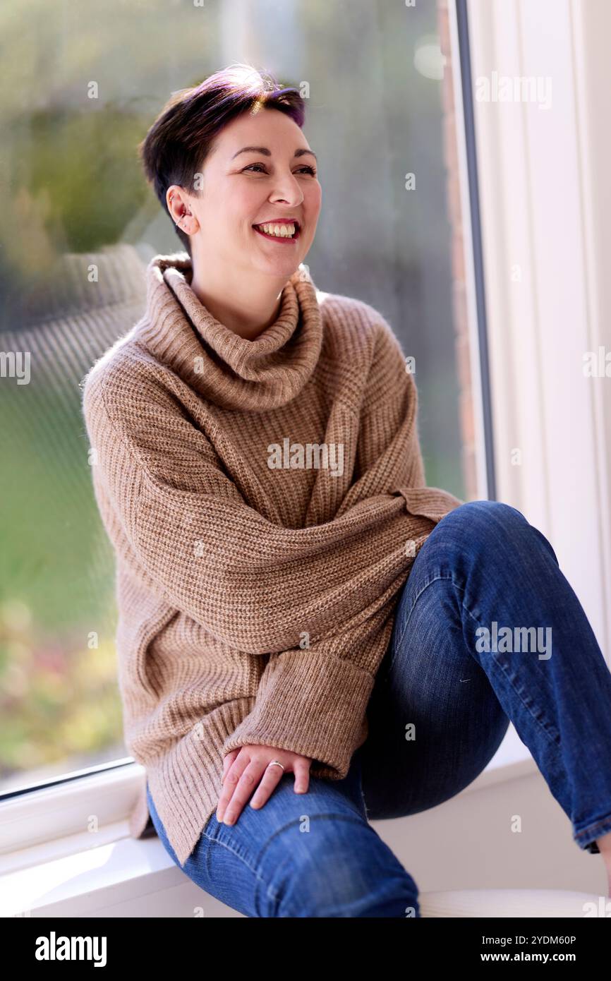 Beautiful woman sat relaxing wearing jeans and jumper Stock Photo - Alamy