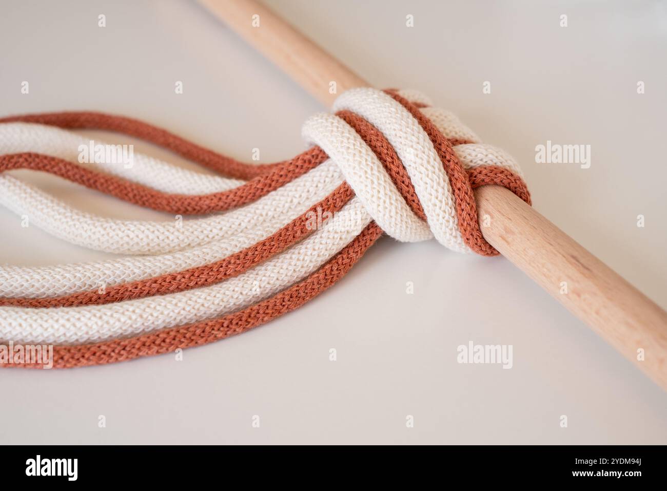 Macrame knot attached to a wooden stick on neutral background. Off ...