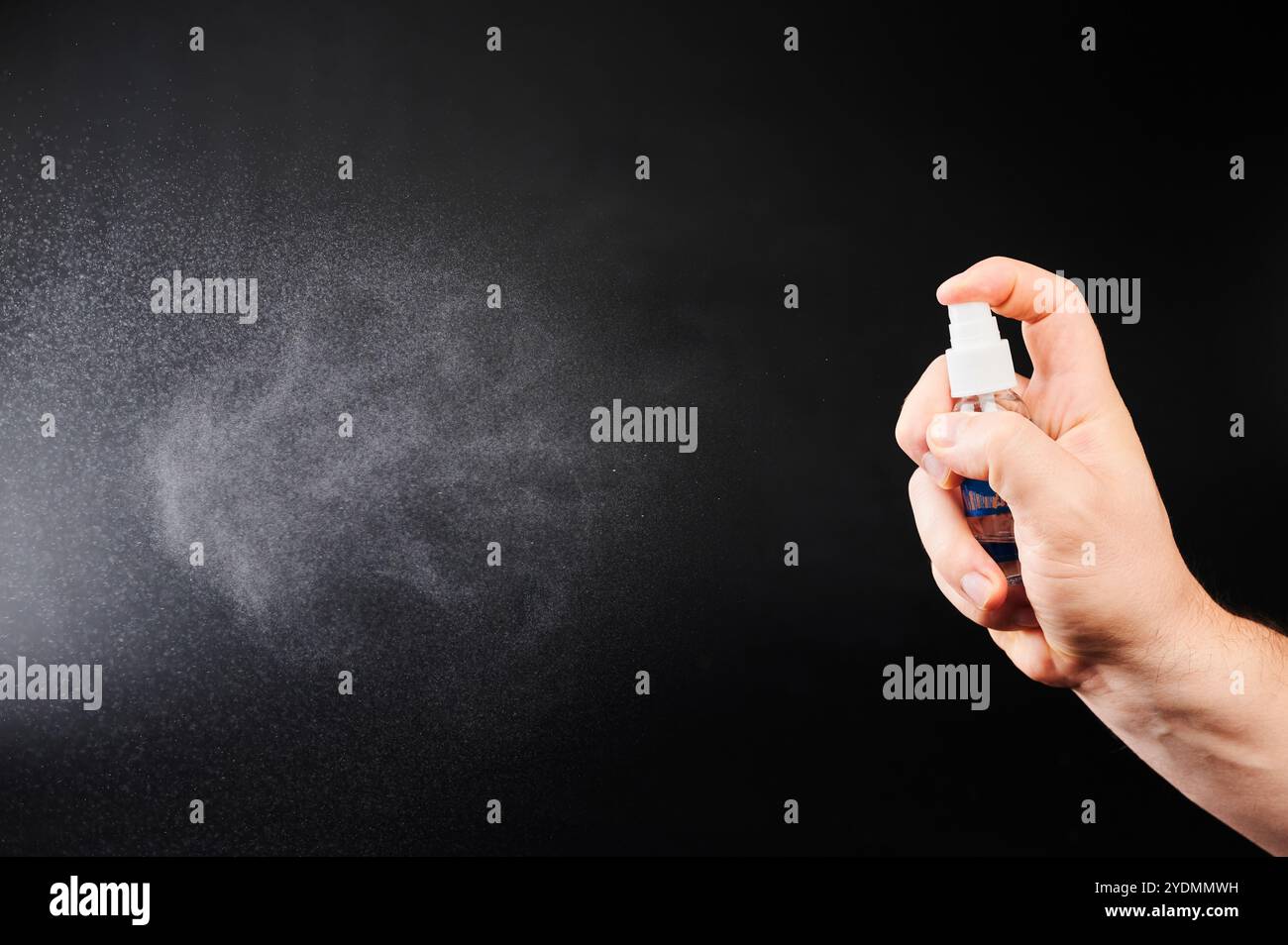 Spray transparent liquid from flask in hand on black studio background ...