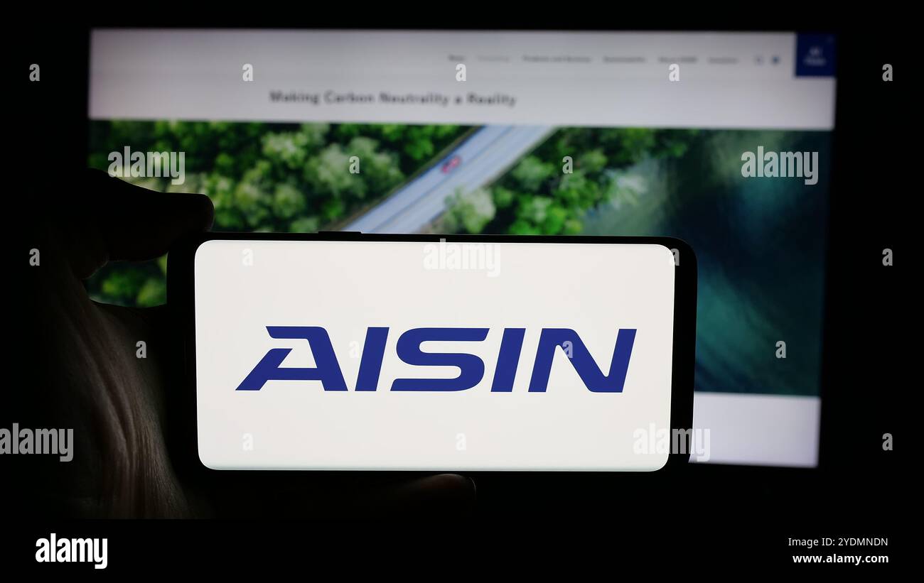 Person holding cellphone with logo of Japanese automotive company Aisin ...