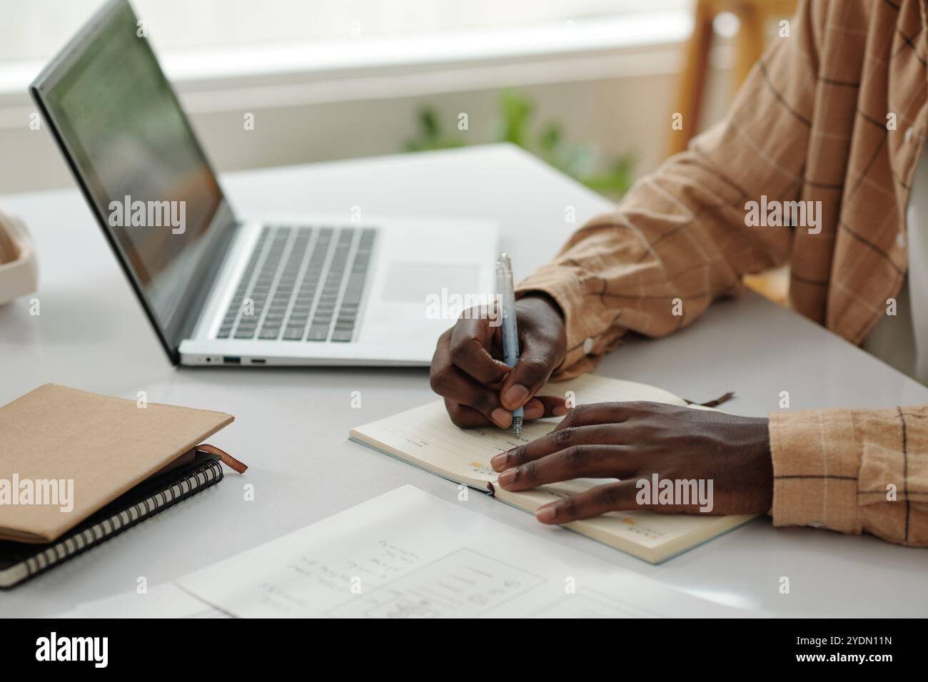 Person taking notes with pen, working alongside an open laptop ...