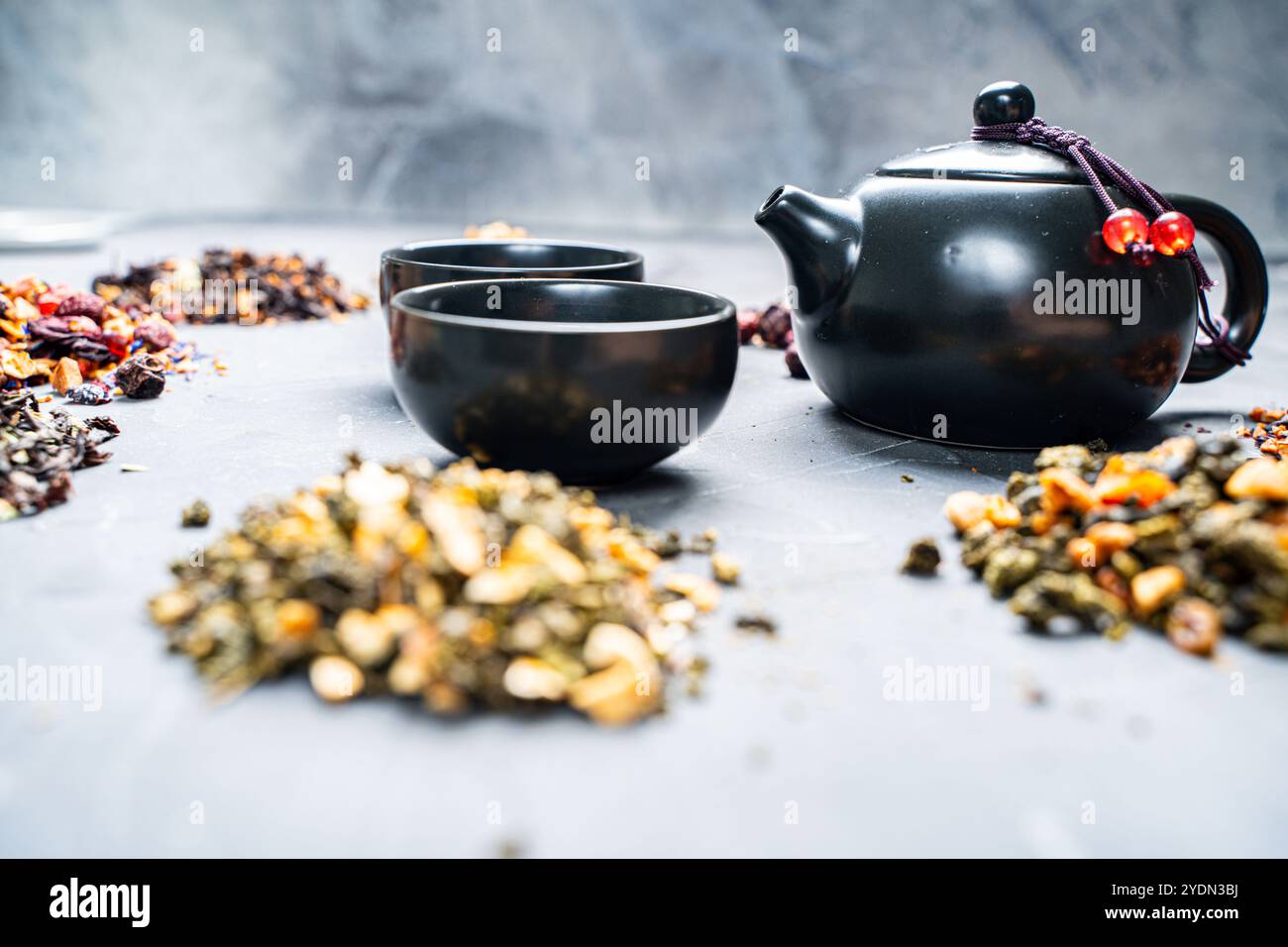 A black teapot and cups on a gray background with scattered tea of ...