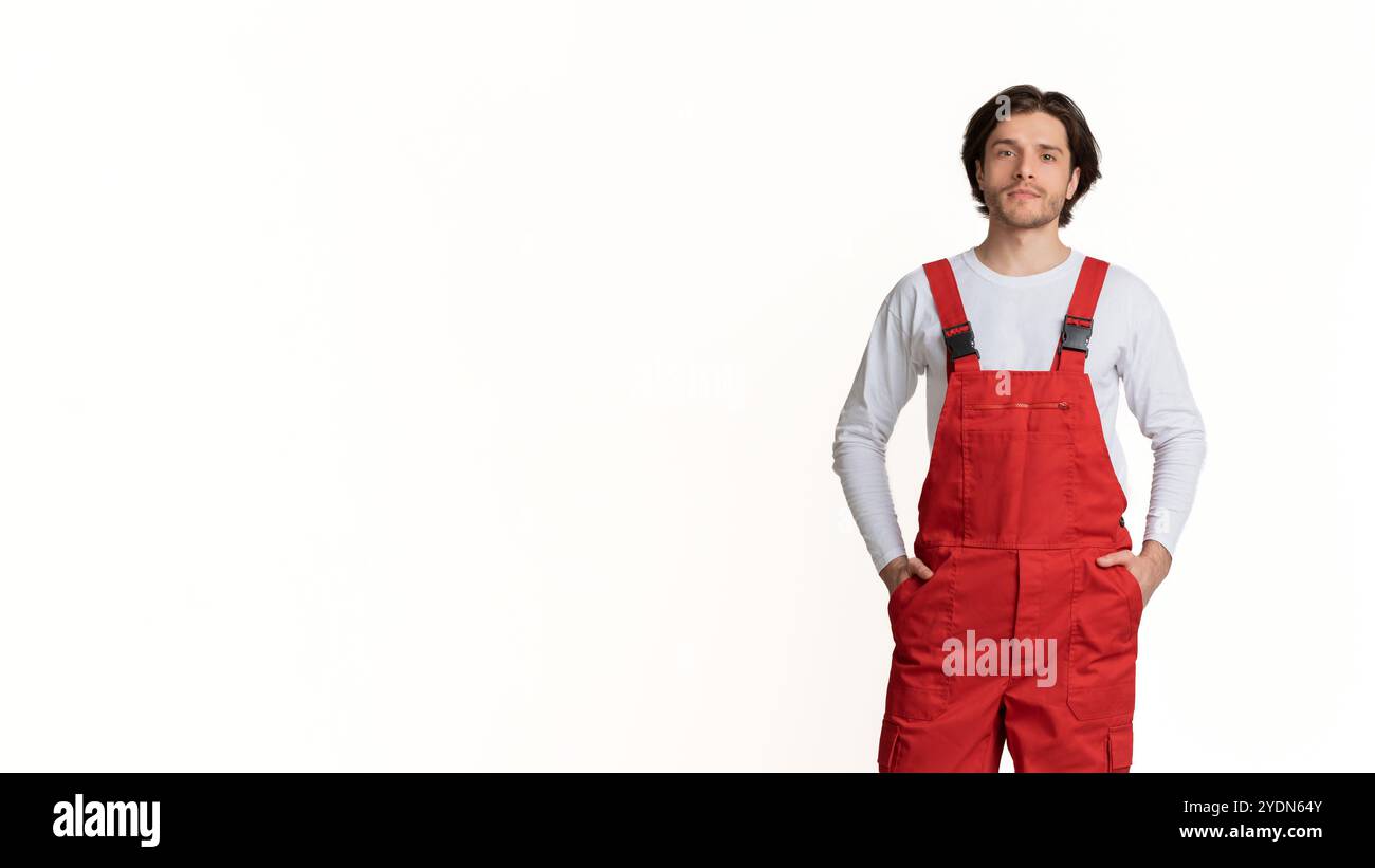 Portrait of young handyman wearing work clothes posing over light ...