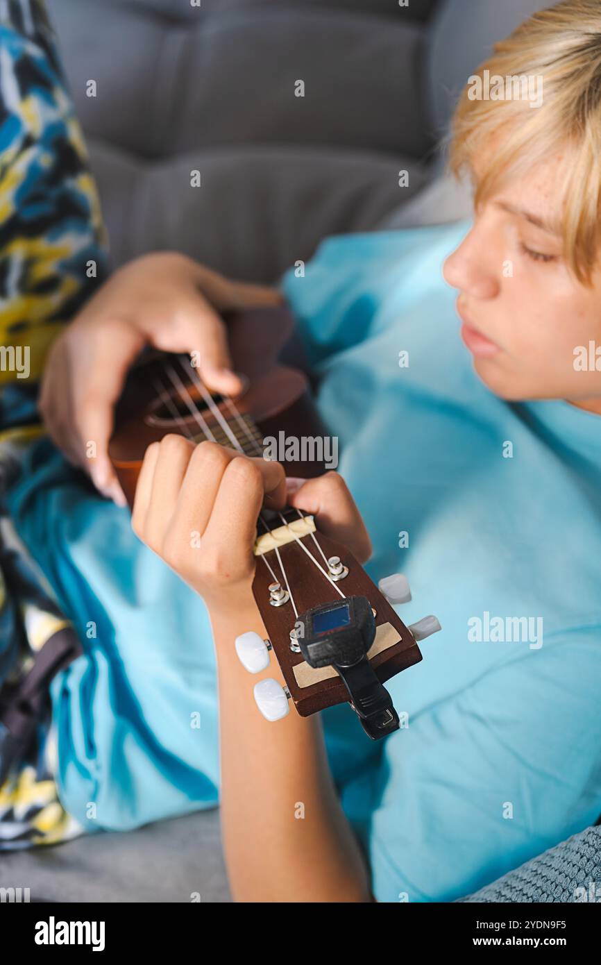Teen boy focuses on playing ukulele guitar, capture moment of musical ...