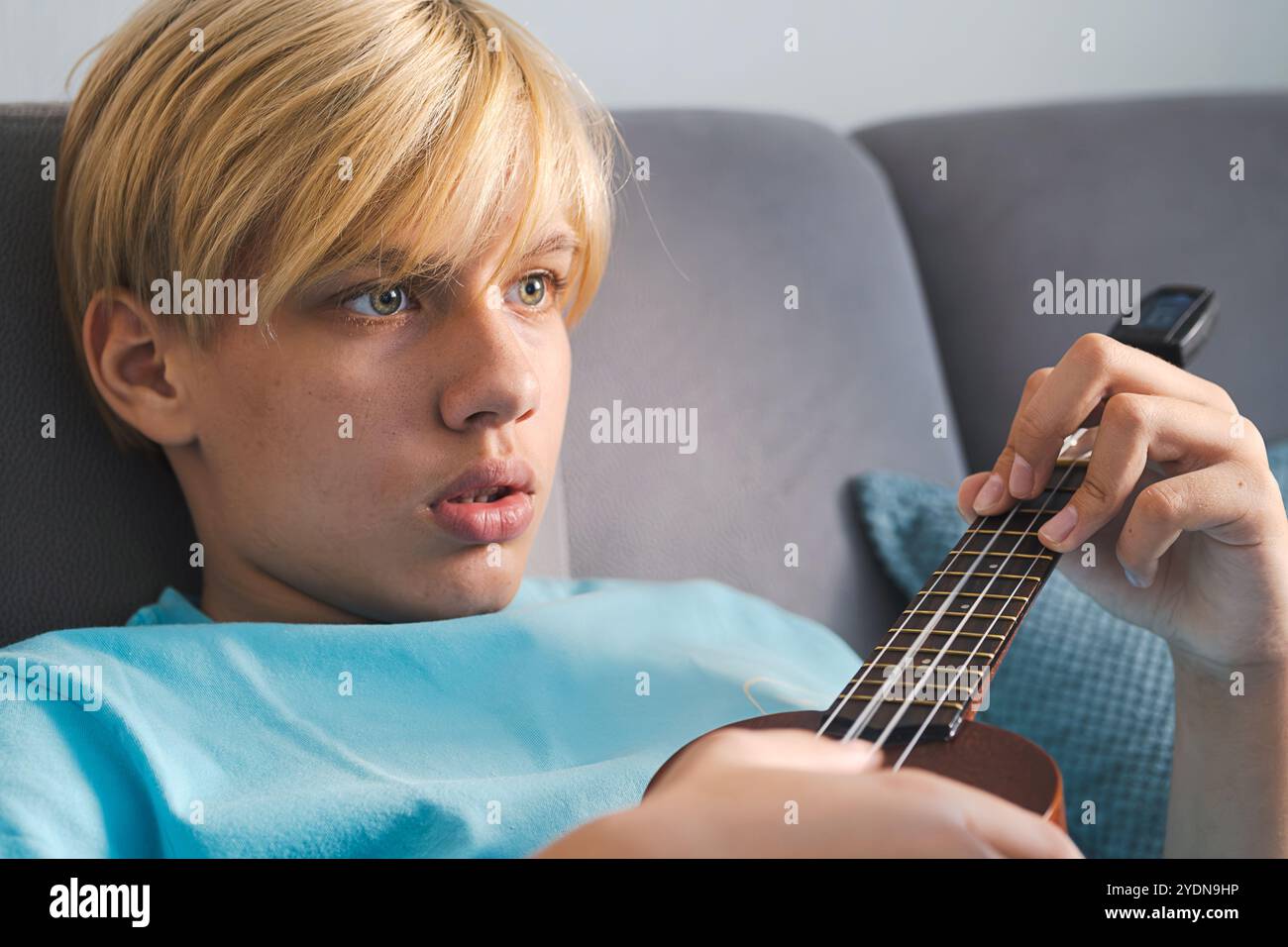 Teen boy focuses on playing ukulele guitar, capture moment of musical ...