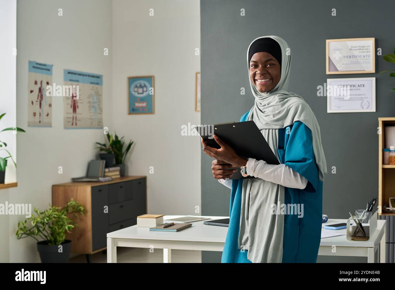 Black Muslim woman in hijab standing in medical office, smiling warmly ...