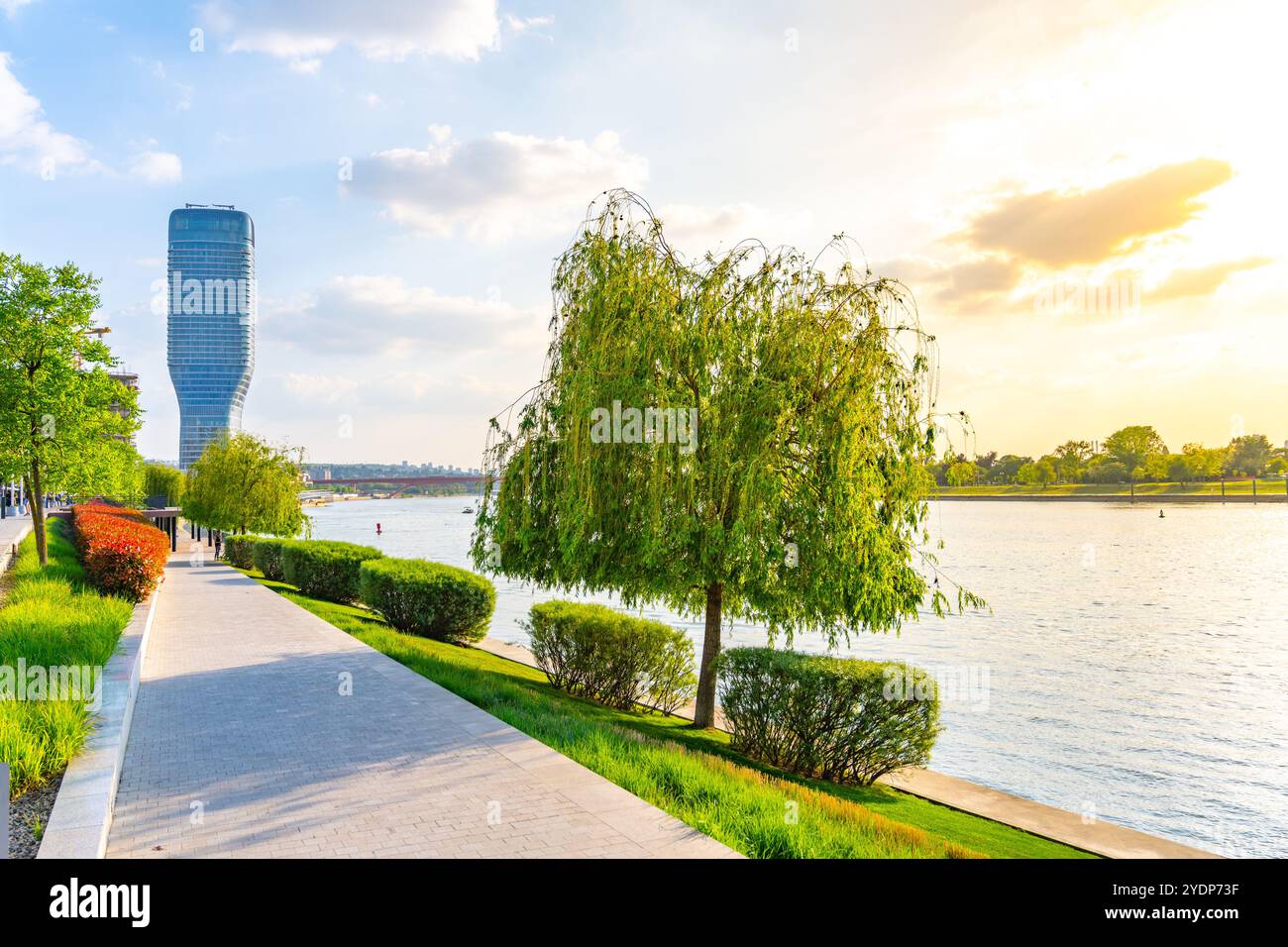 A sunny riverside pathway lined with greenery offers a clear view of ...