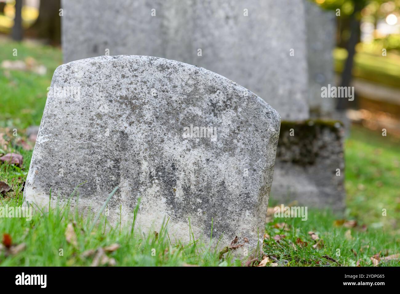 A closeup of a small old tombstone. The stone is blank, a larger stone ...