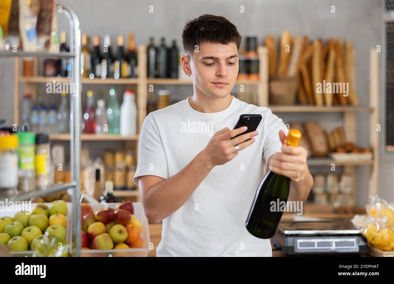 Young guy purchaser scanning with smartphone QR code label of bottle of ...