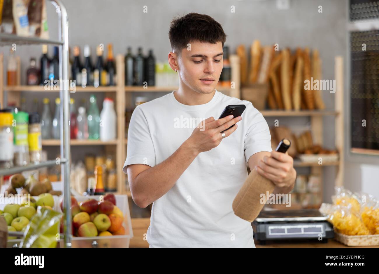 Young guy purchaser scanning with smartphone QR code label of bottle of ...