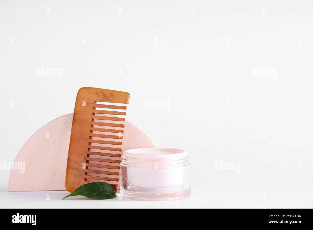 Plaster podium with jar of hair mask, comb and leaf on white background ...