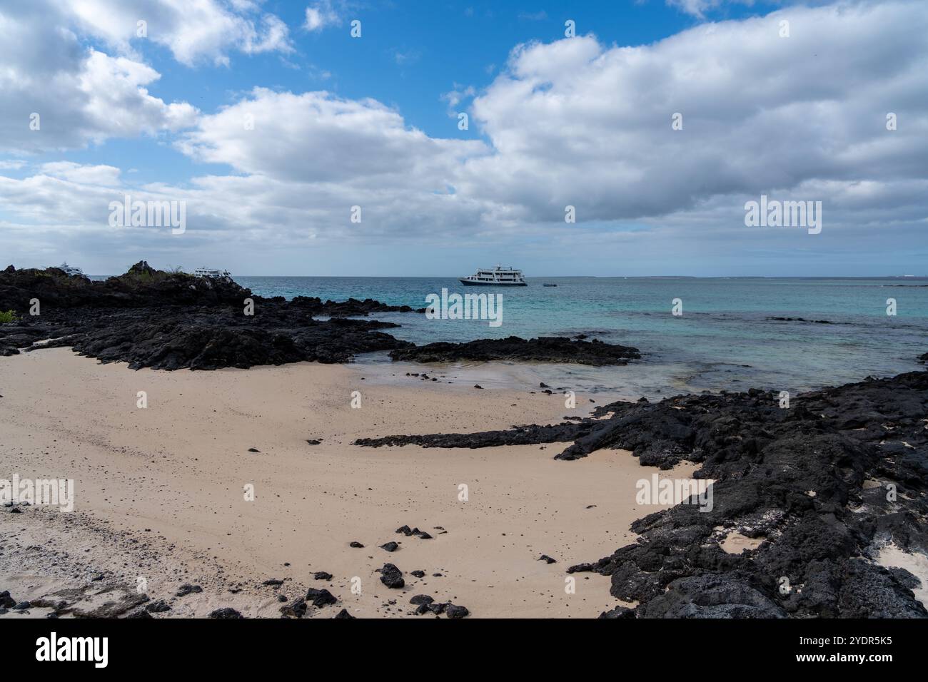 Empty galapagos sand and lava rock beach with a tour boat in the ...