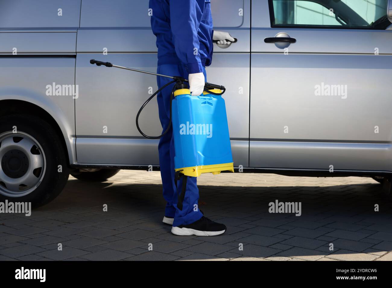 Pest control worker with spray tank near gray minibus outdoors, closeup ...