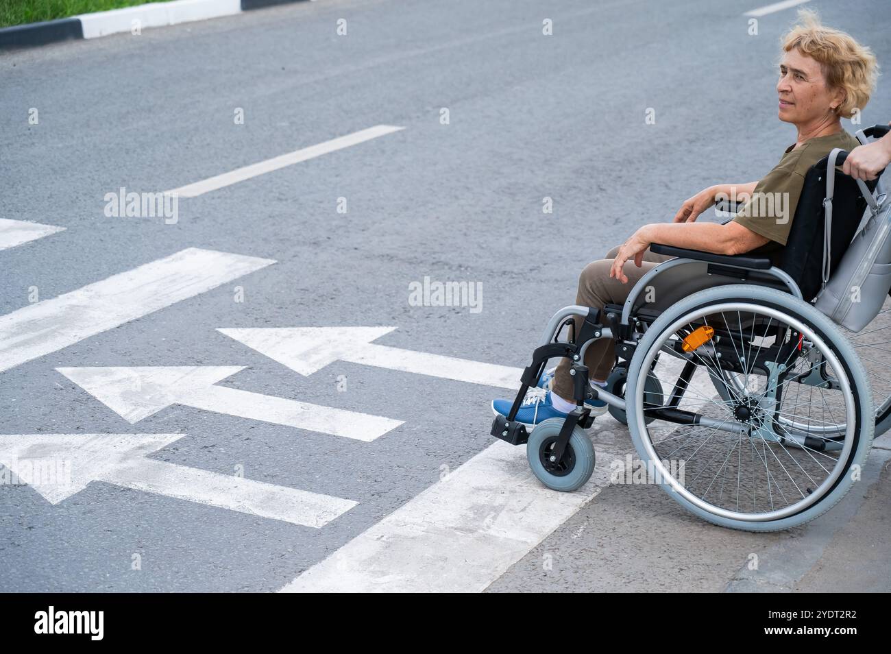 Profile of a nurse helping an elderly woman in a wheelchair cross the ...