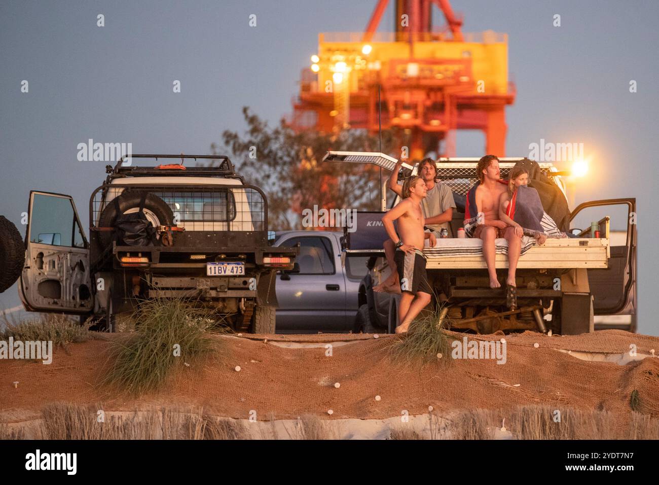 This image depicts a group of people gathered at the back of two pickup ...