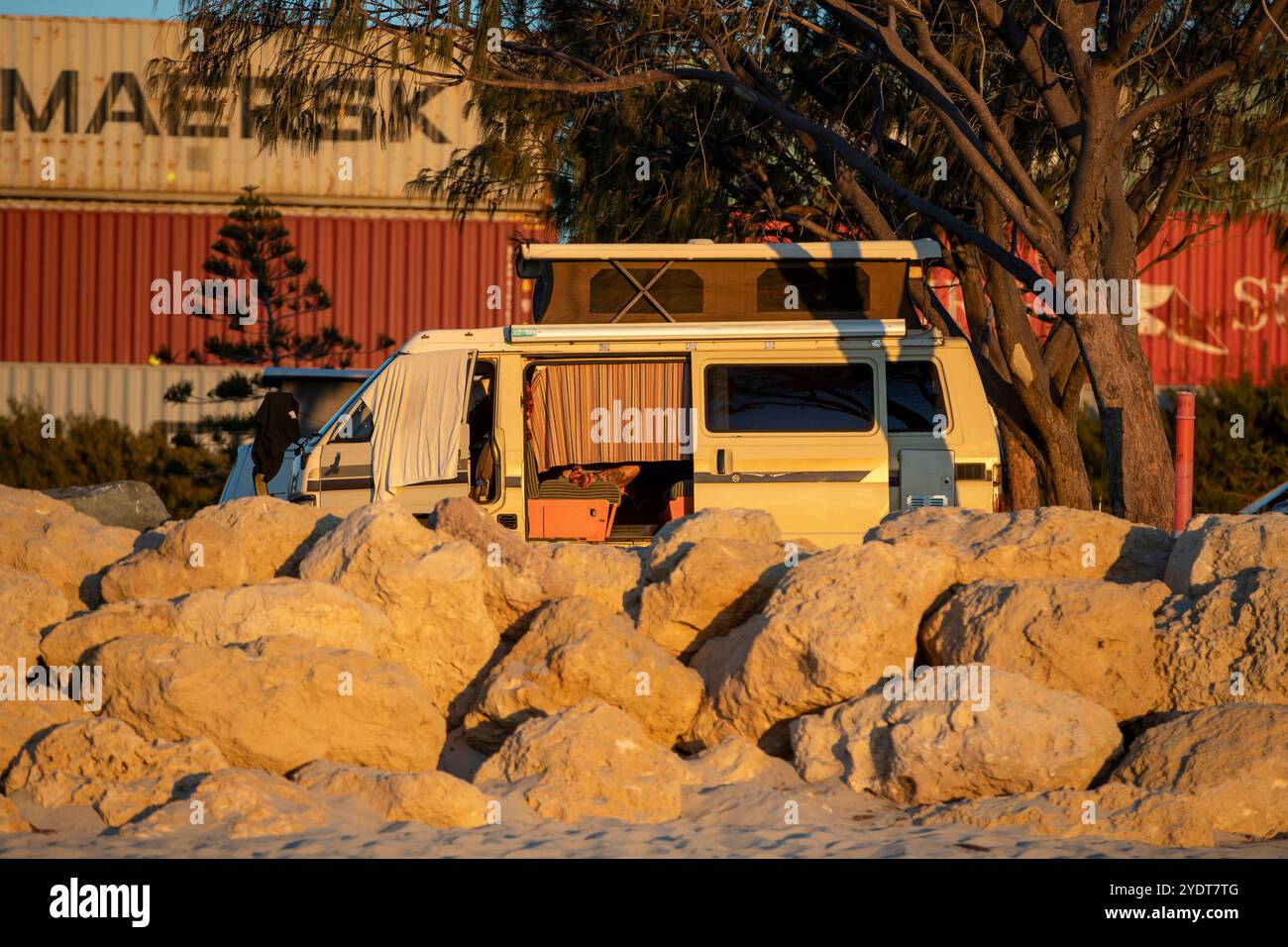 This image depicts a classic camper van parked behind a set of large ...