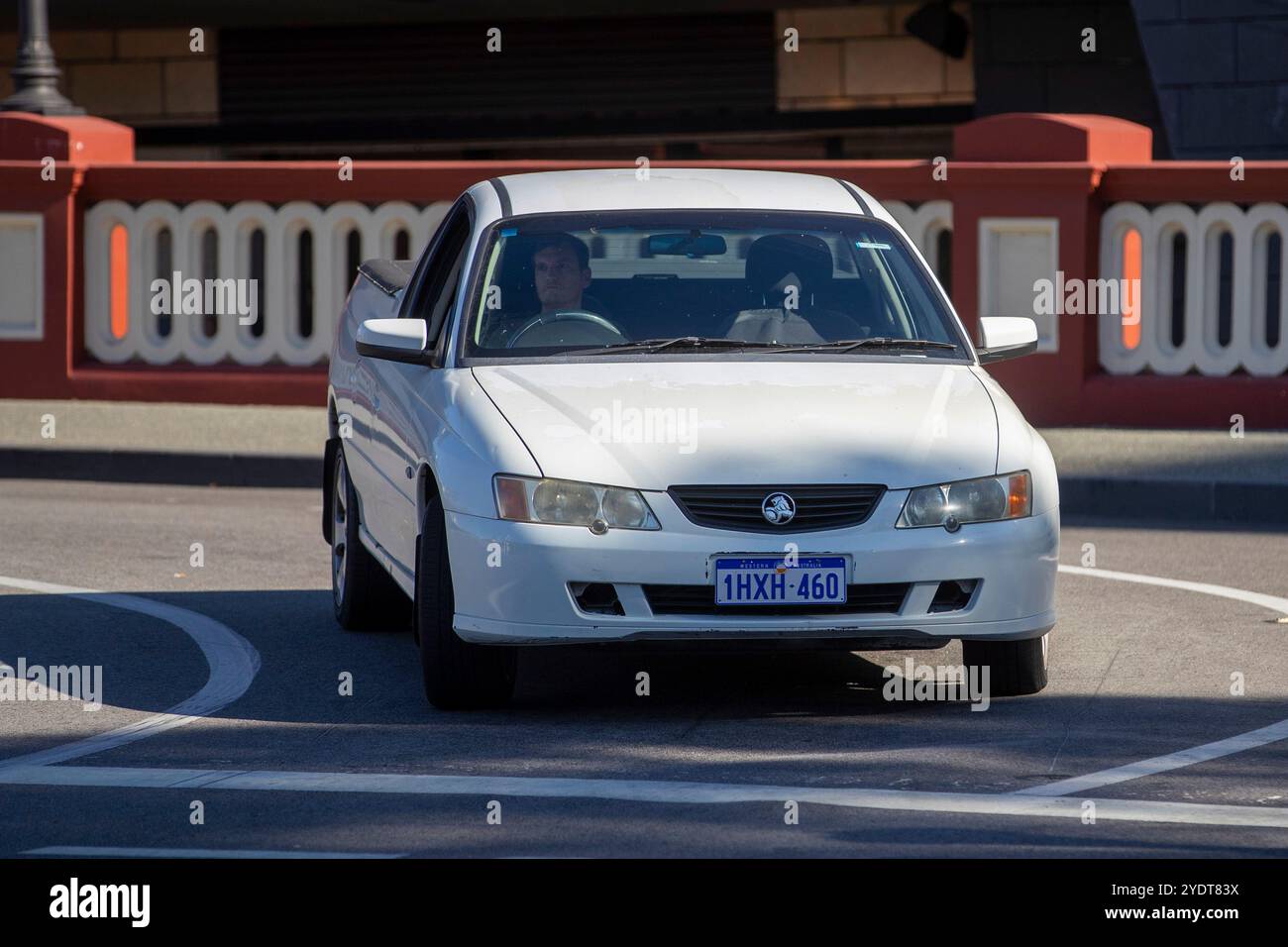A white Holden ute car driving on a street, with a person visible ...