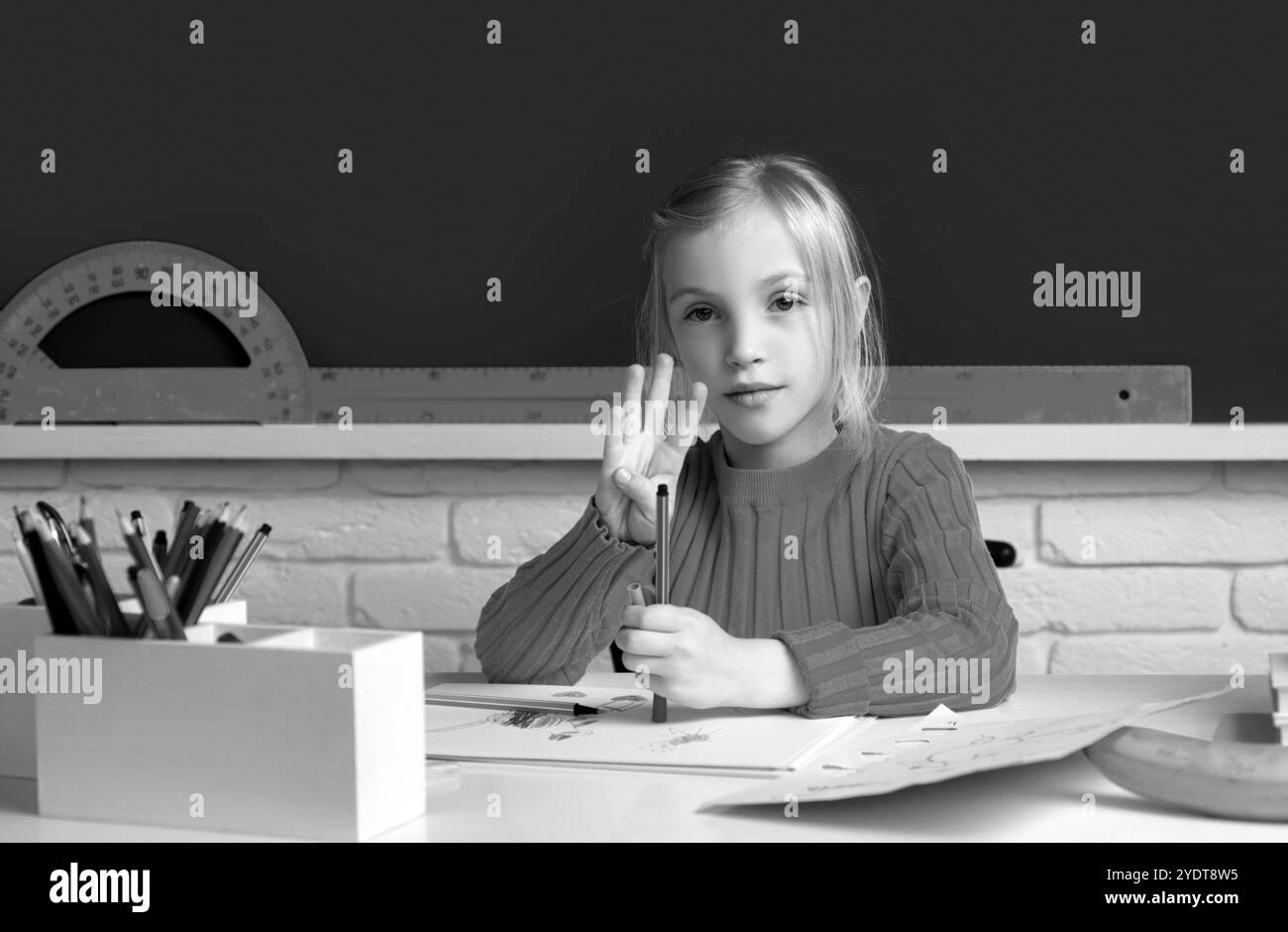 Portrait of cute little schoolgirl writing in book with classmates in ...