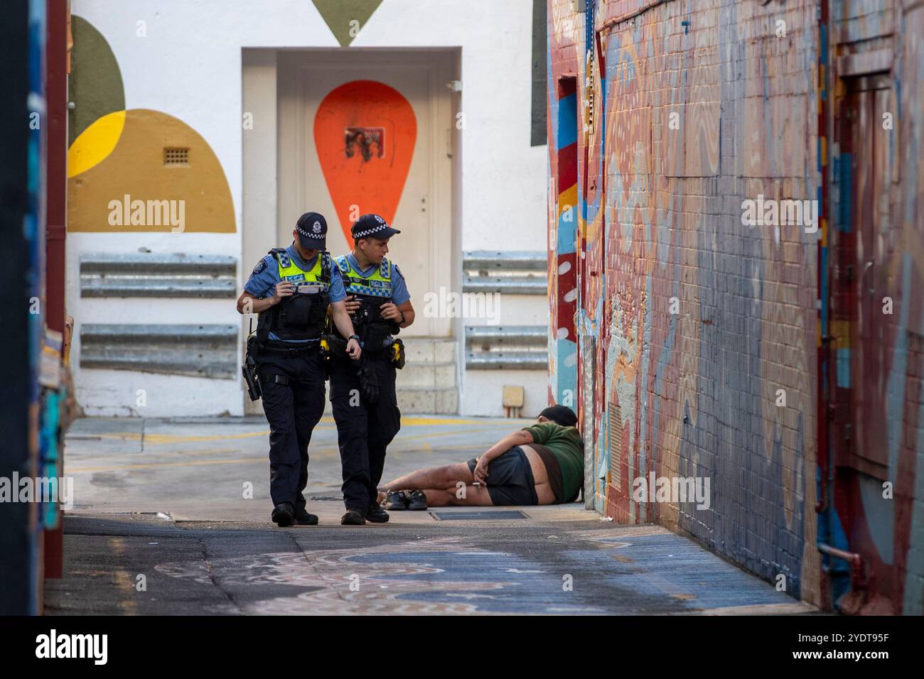 Two police officers walking through a graffiti-decorated alleyway where ...