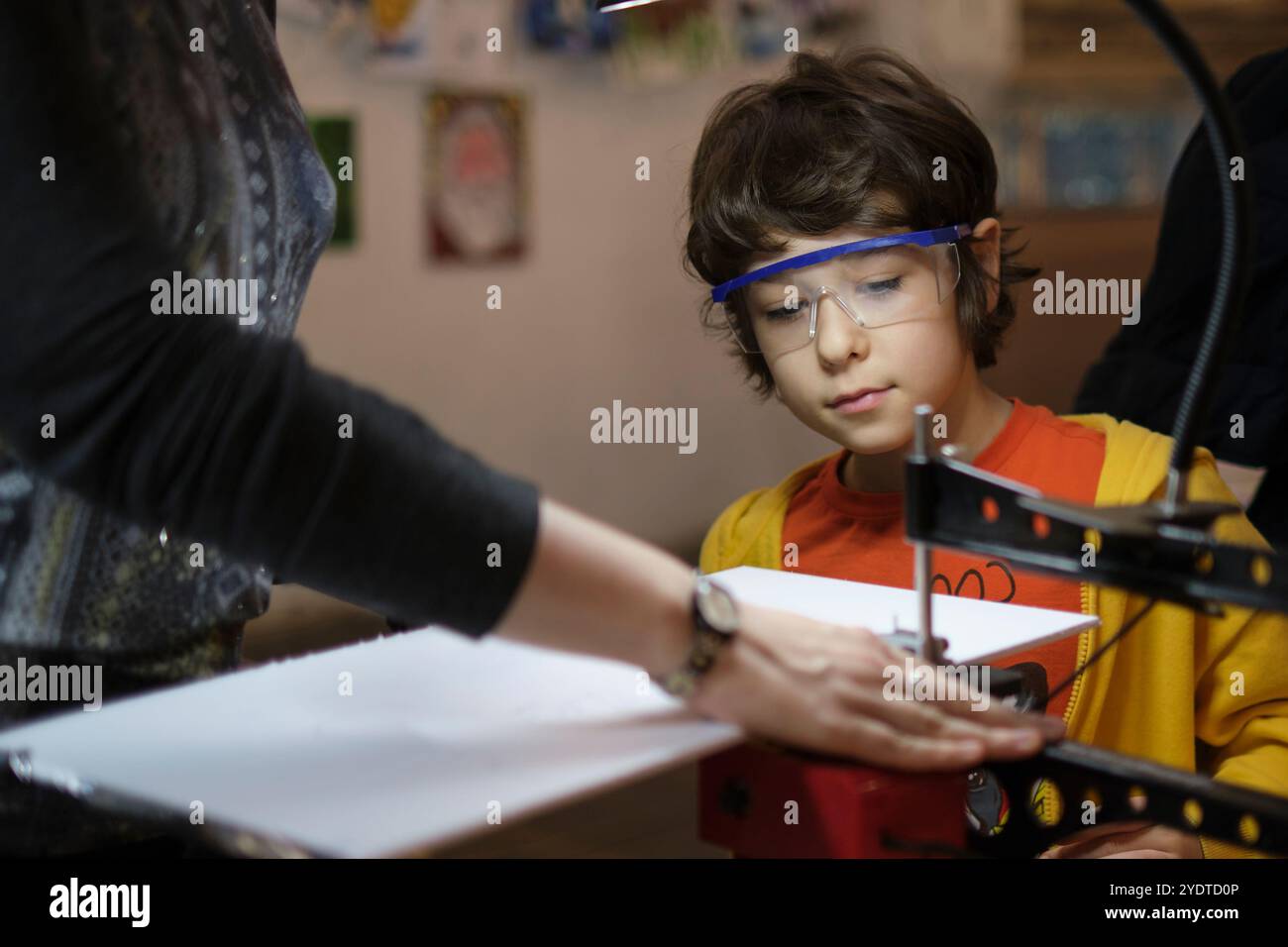 young boy meticulously carves wood on a lathe, under the careful ...