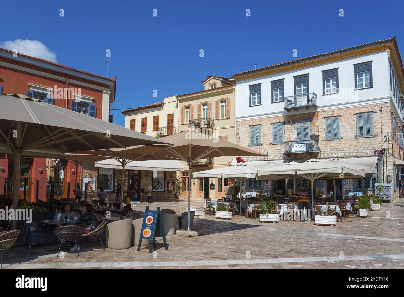 Lively street cafe with large parasols and colourful buildings under a ...