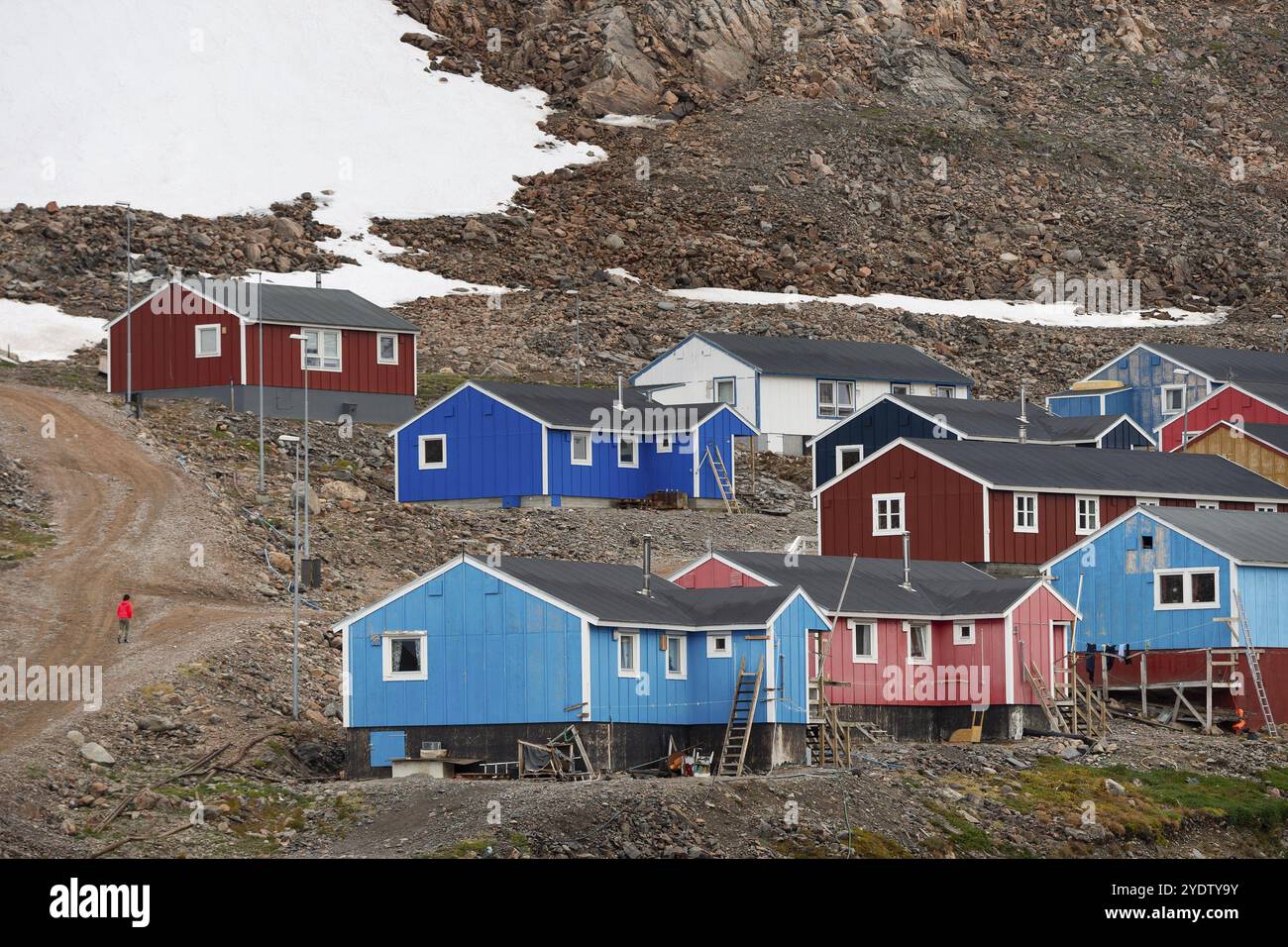 Gravel road and colourful wooden houses on a slope with snow remains ...