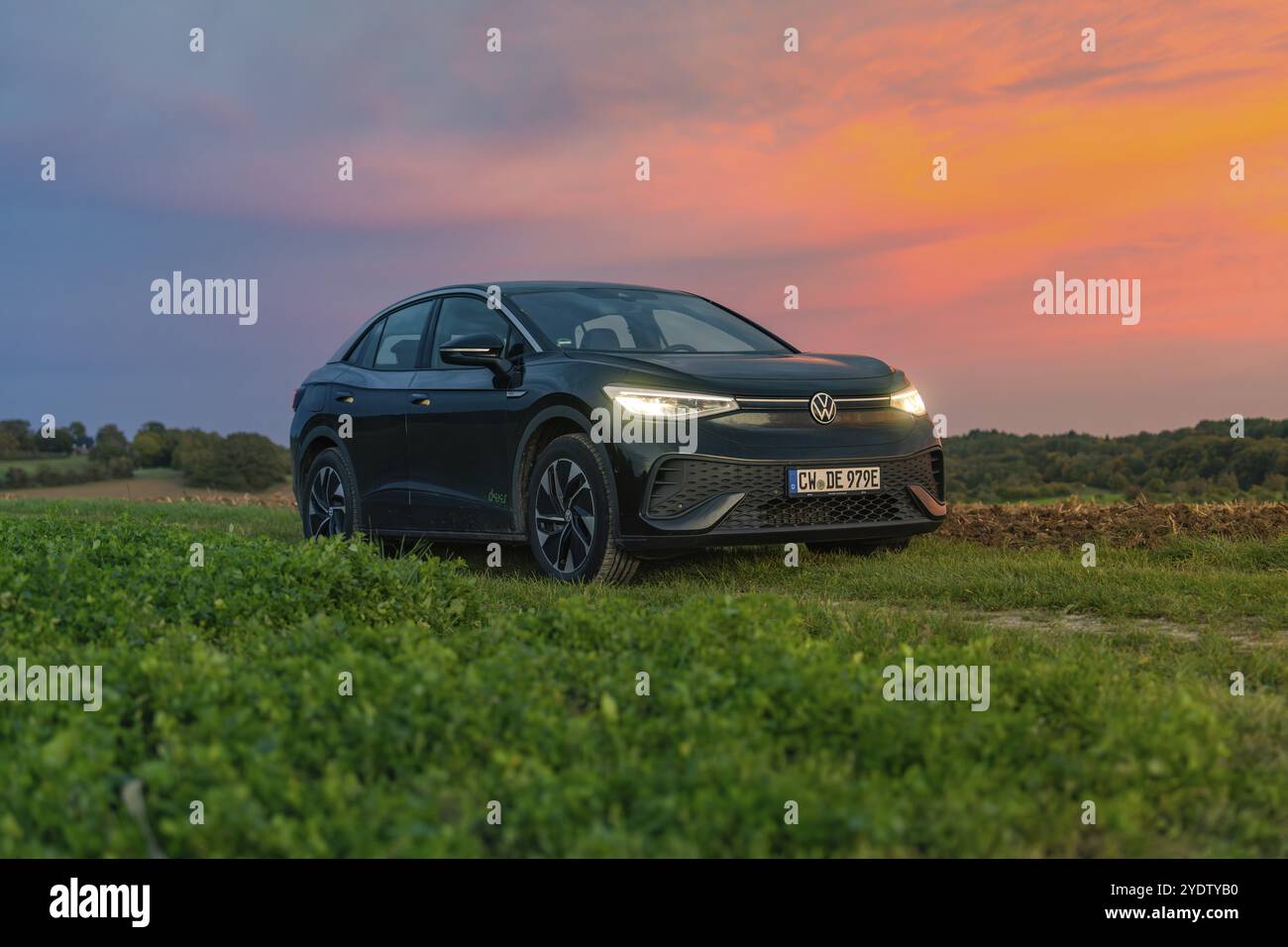 A car stands in front of a dramatic sunset in a field with a colourful ...