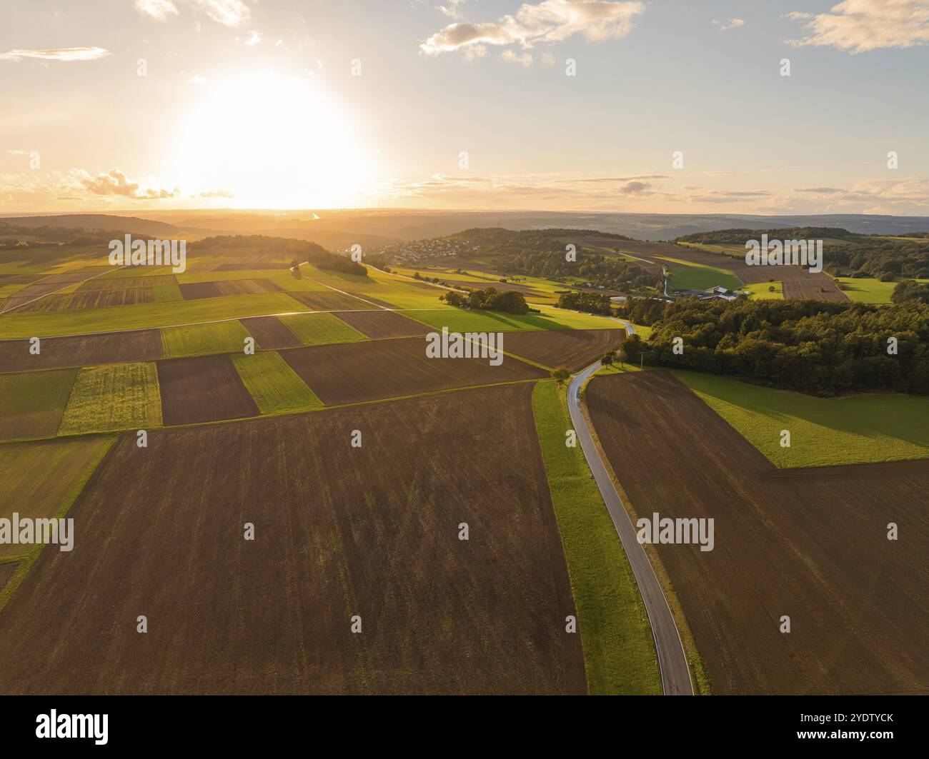 Sunset over sweeping fields with a winding road and dramatic sky ...