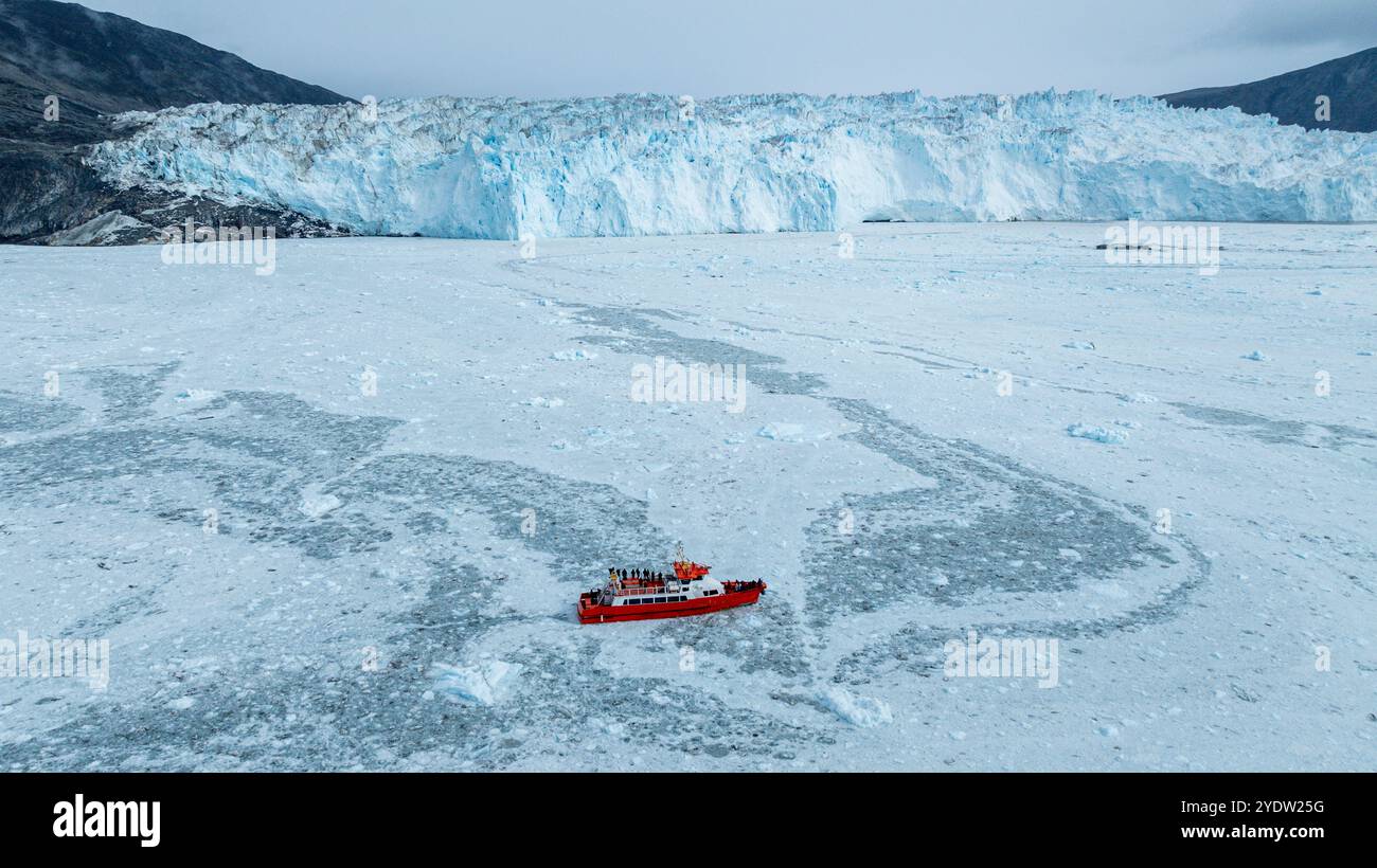 Aerial of a little ship floating between the ice below the Eqi glacier ...